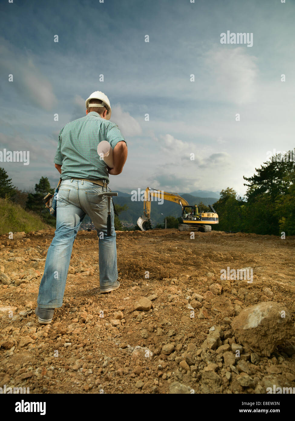 back view of engineer holding blueprint, walking on construction site ...