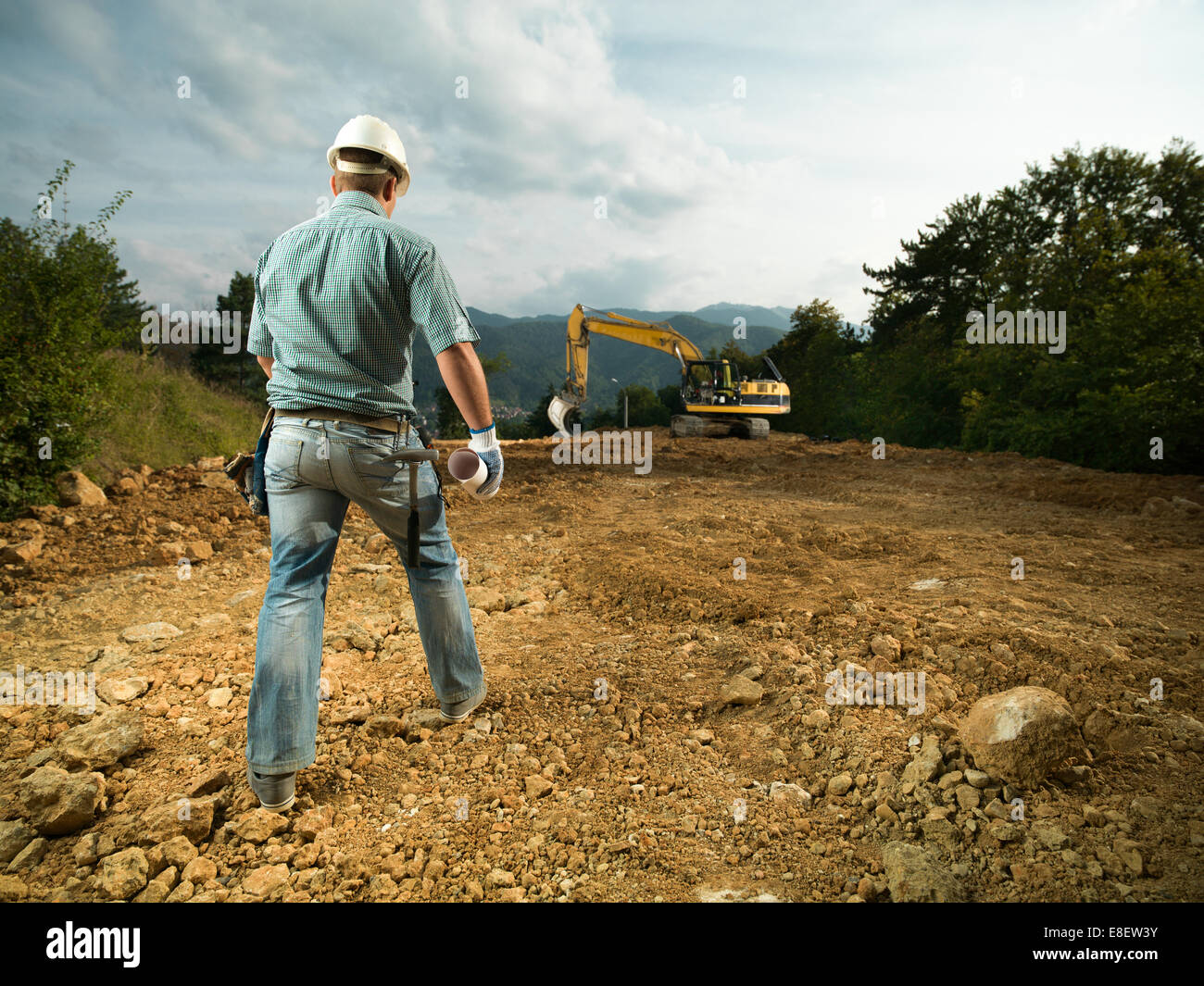back view of engineer holding blueprint , walking on construction site ...