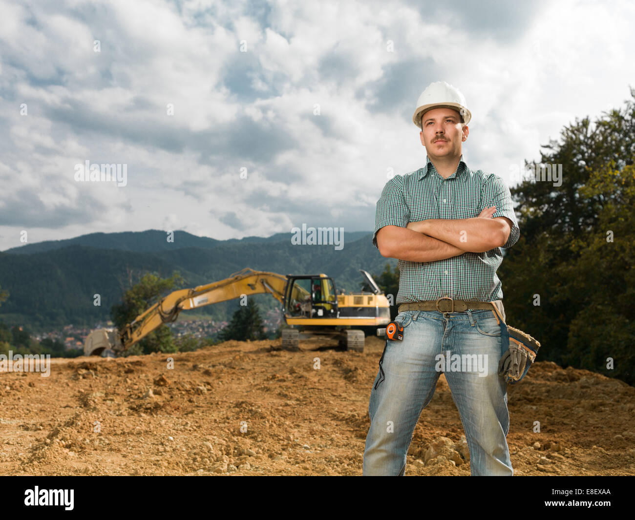 male engineer standing on construction site with excavator in ...