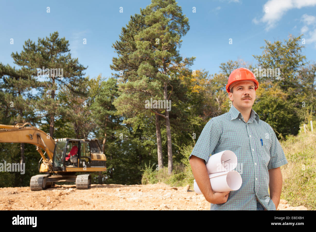 side view of standing engineer holding blueprints on construction site ...