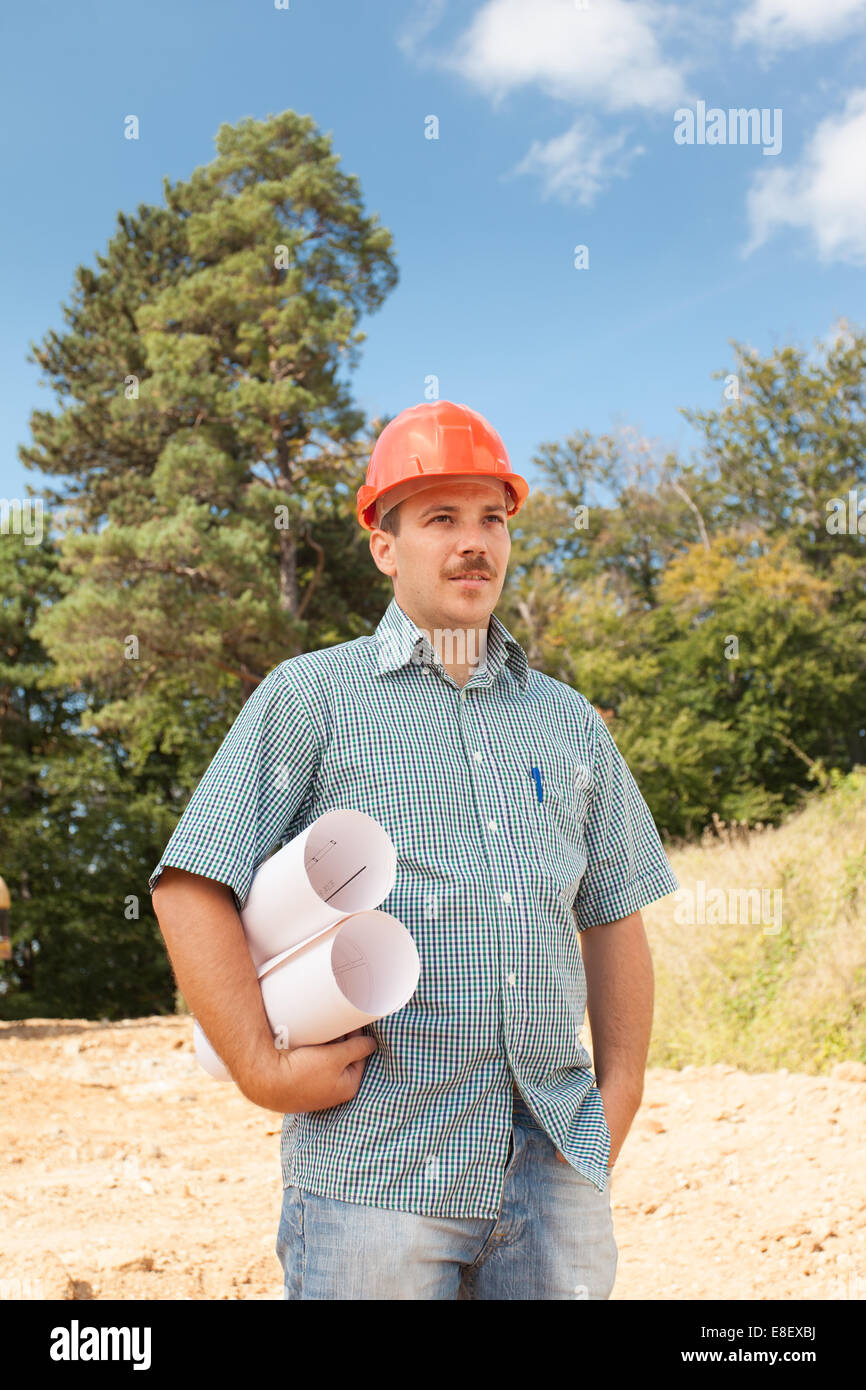side view of standing engineer holding blueprints on construction site ...