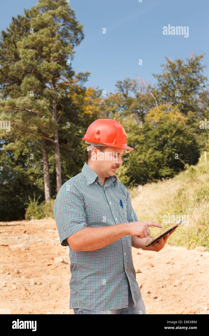 side view of standing engineer holding tablet on construction site ...