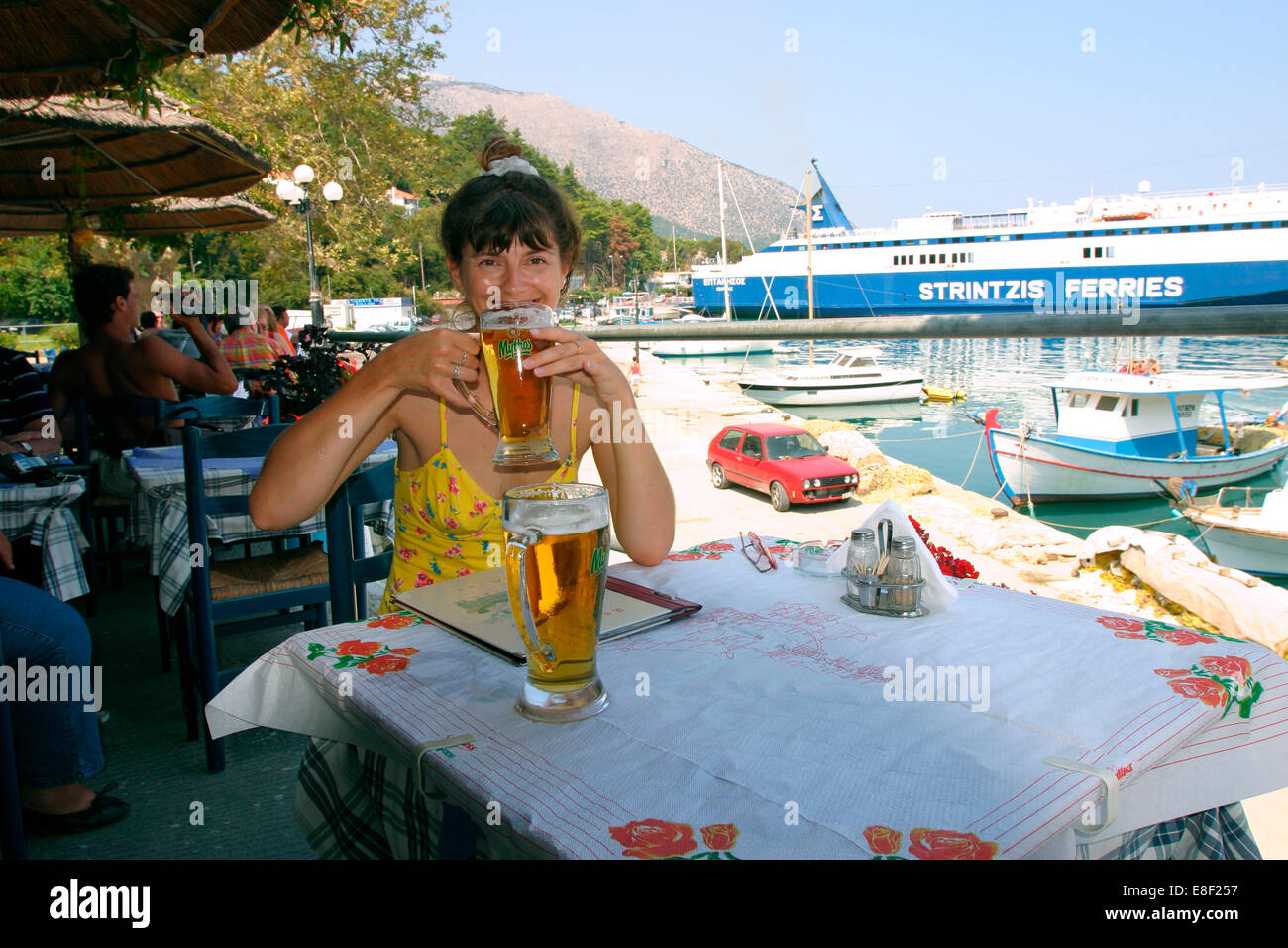 Woman enjoying a drink in a harbourside taverna, Poros, Kefalonia ...