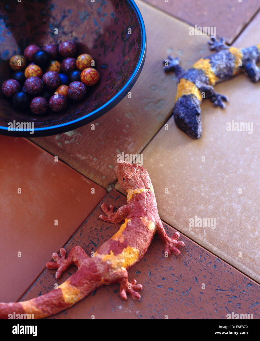 Close-up of blue and pink clay lizards beside bowl of marbles on tiled ...