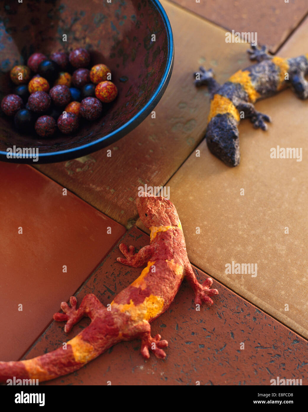 Close-up of orange and blue Fimo lizards beside marbles in blue bowl ...