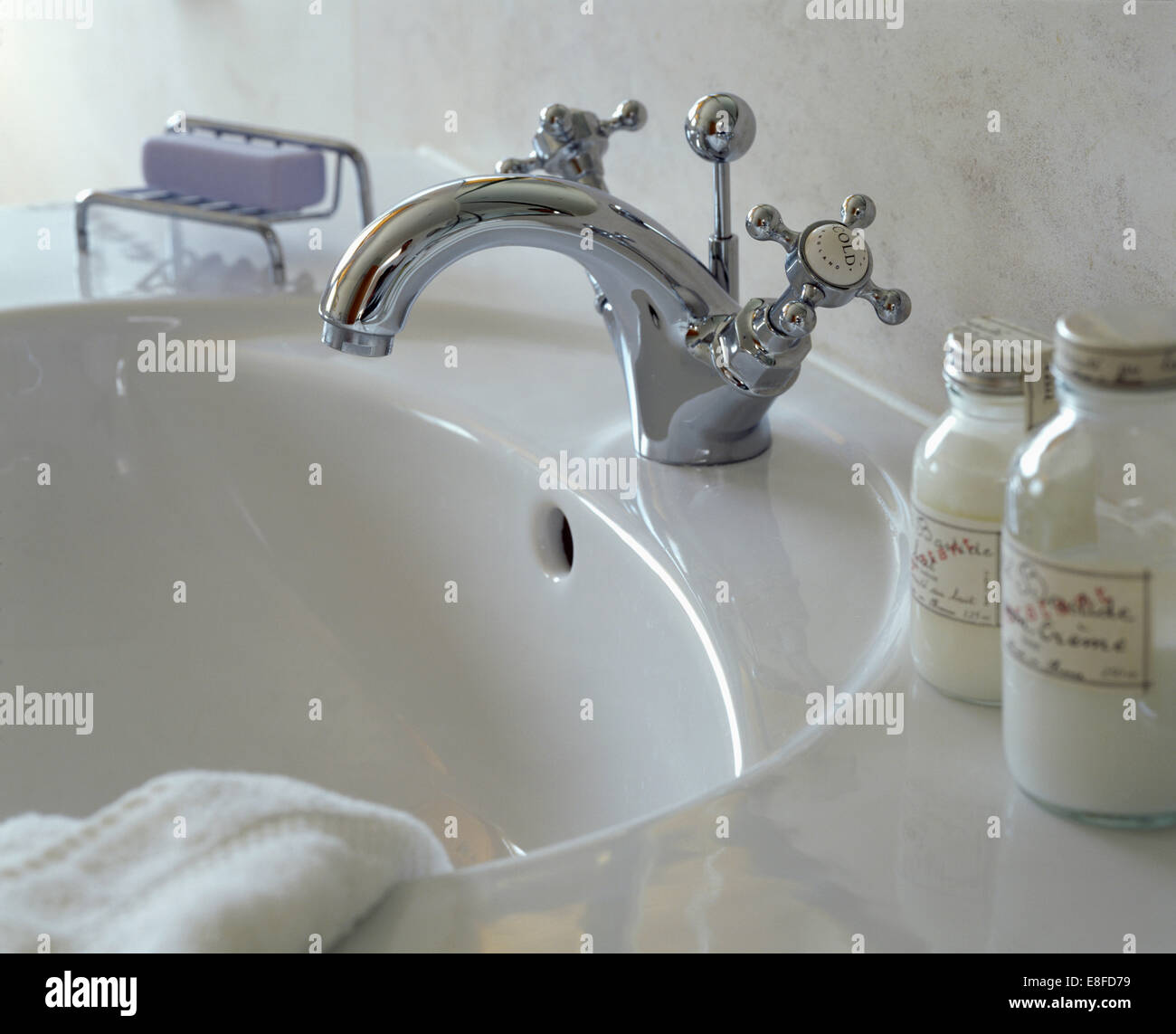 Chrome mixer tap on white porcelain basin with bottles of toiletries ...