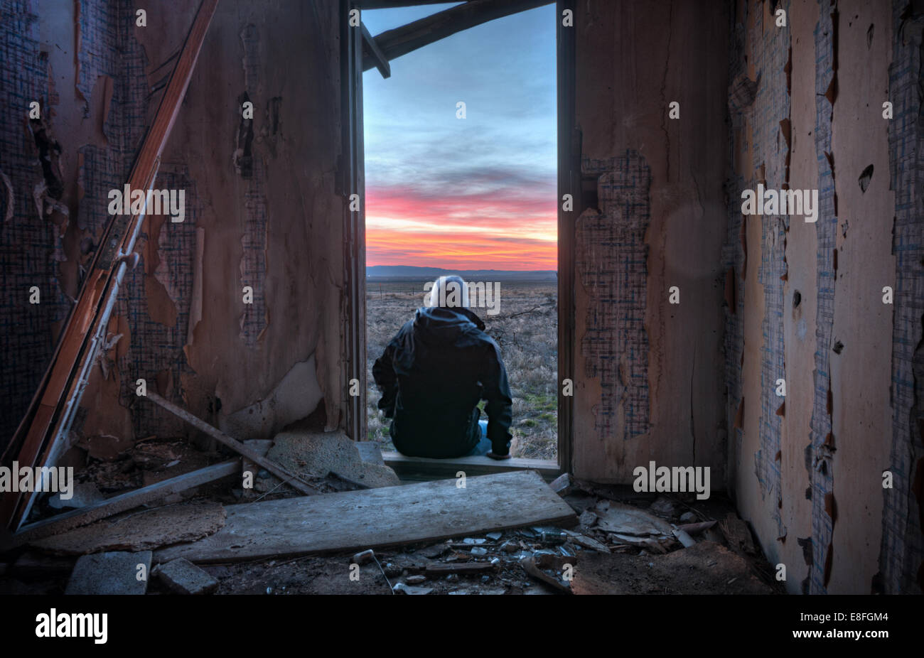 USA, Idaho, Rear view of man sitting on doorstep looking at sunset ...