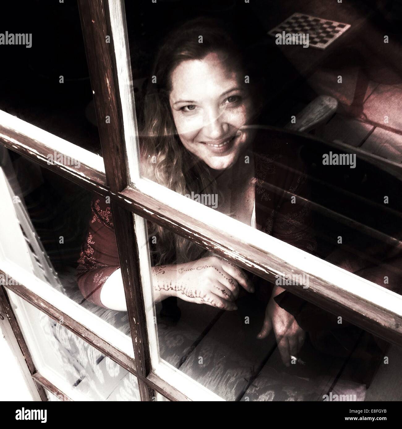 Smiling Woman sitting by a window smoking Stock Photo - Alamy