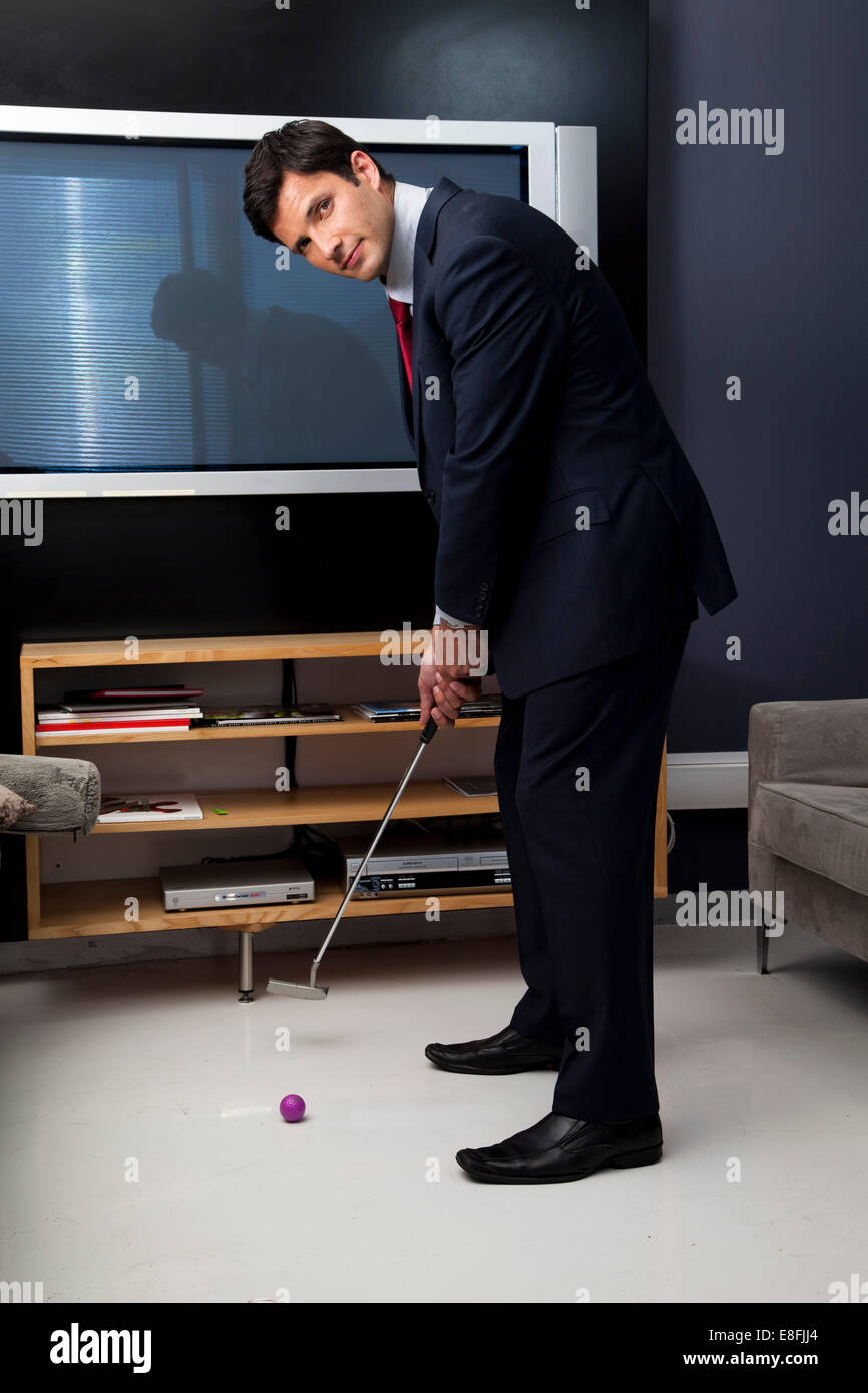 Businessman putting golf ball in office Stock Photo - Alamy