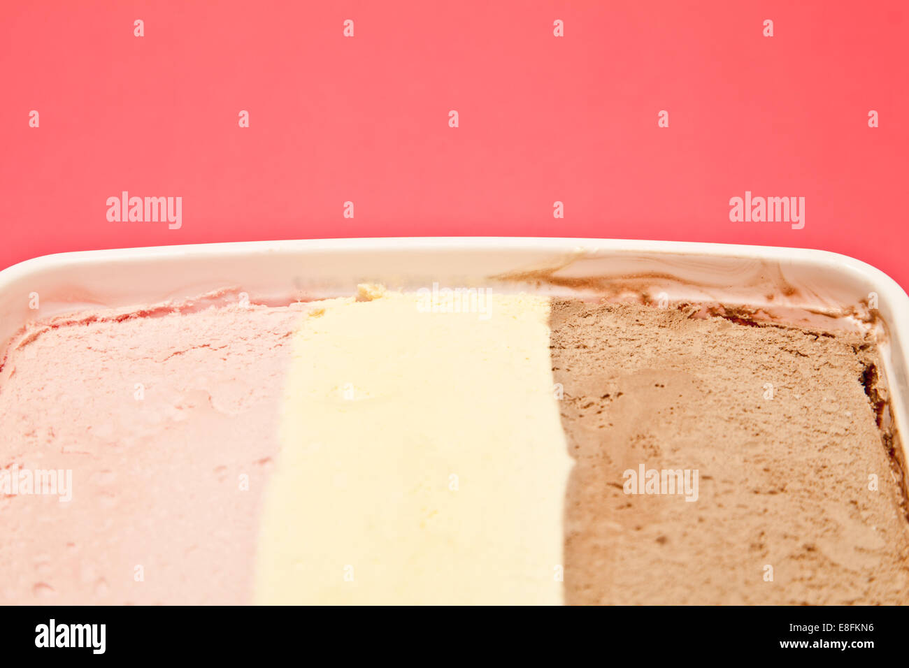 Close-Up of a tub of neapolitan Ice Cream against a pink background ...