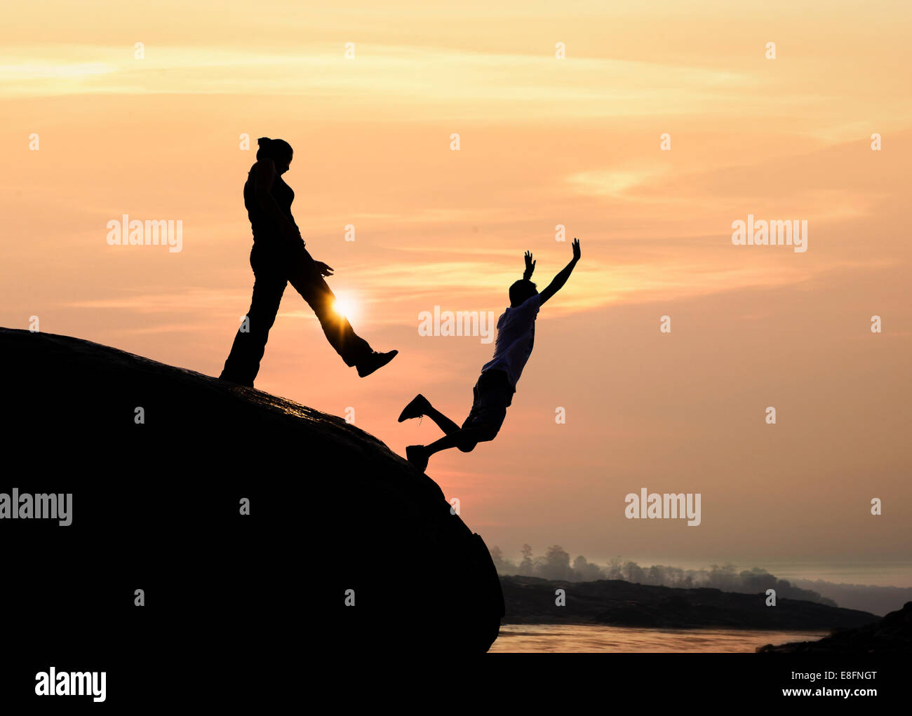 Silhouette of a man standing on rock kicking a woman Stock Photo - Alamy