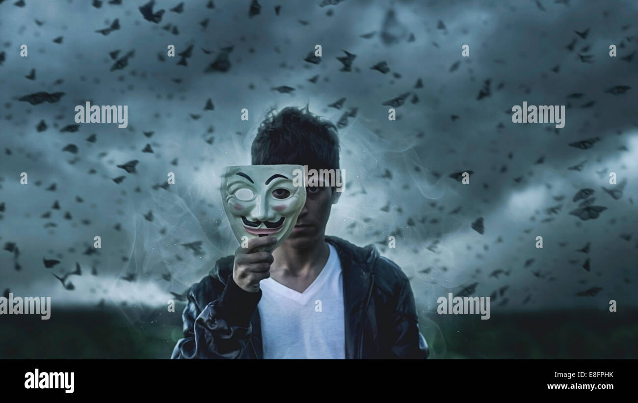 Portrait of a Man holding a carnival mask in front of his face with ...