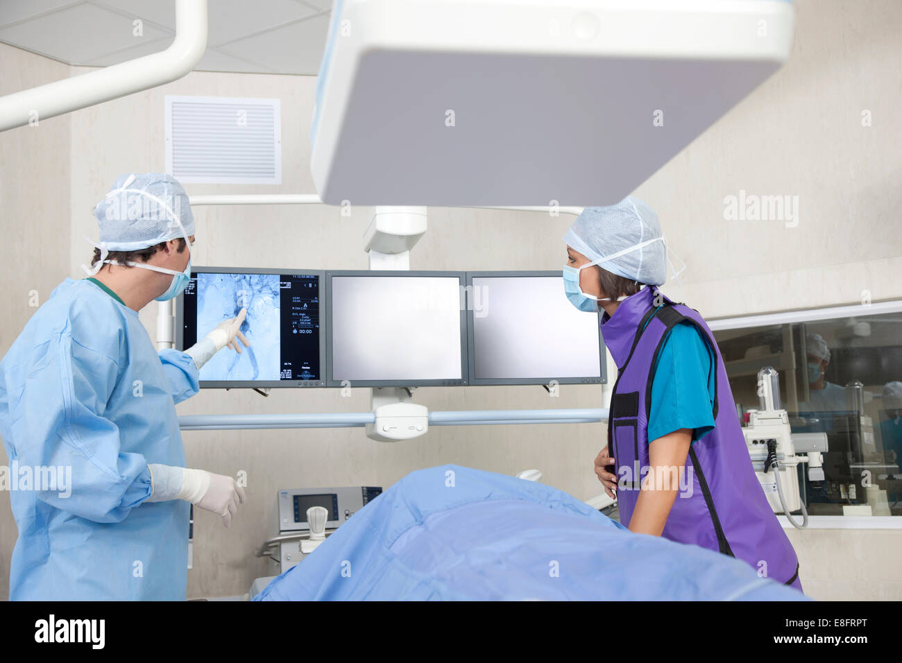 Surgeon and nurse analysing MRI scan with patient in operating theatre ...