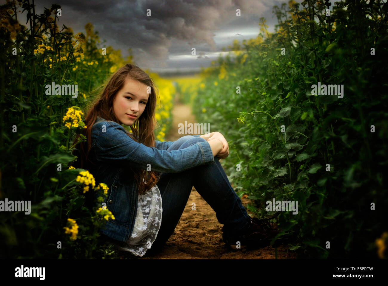 Side view of girl sitting in field Stock Photo - Alamy