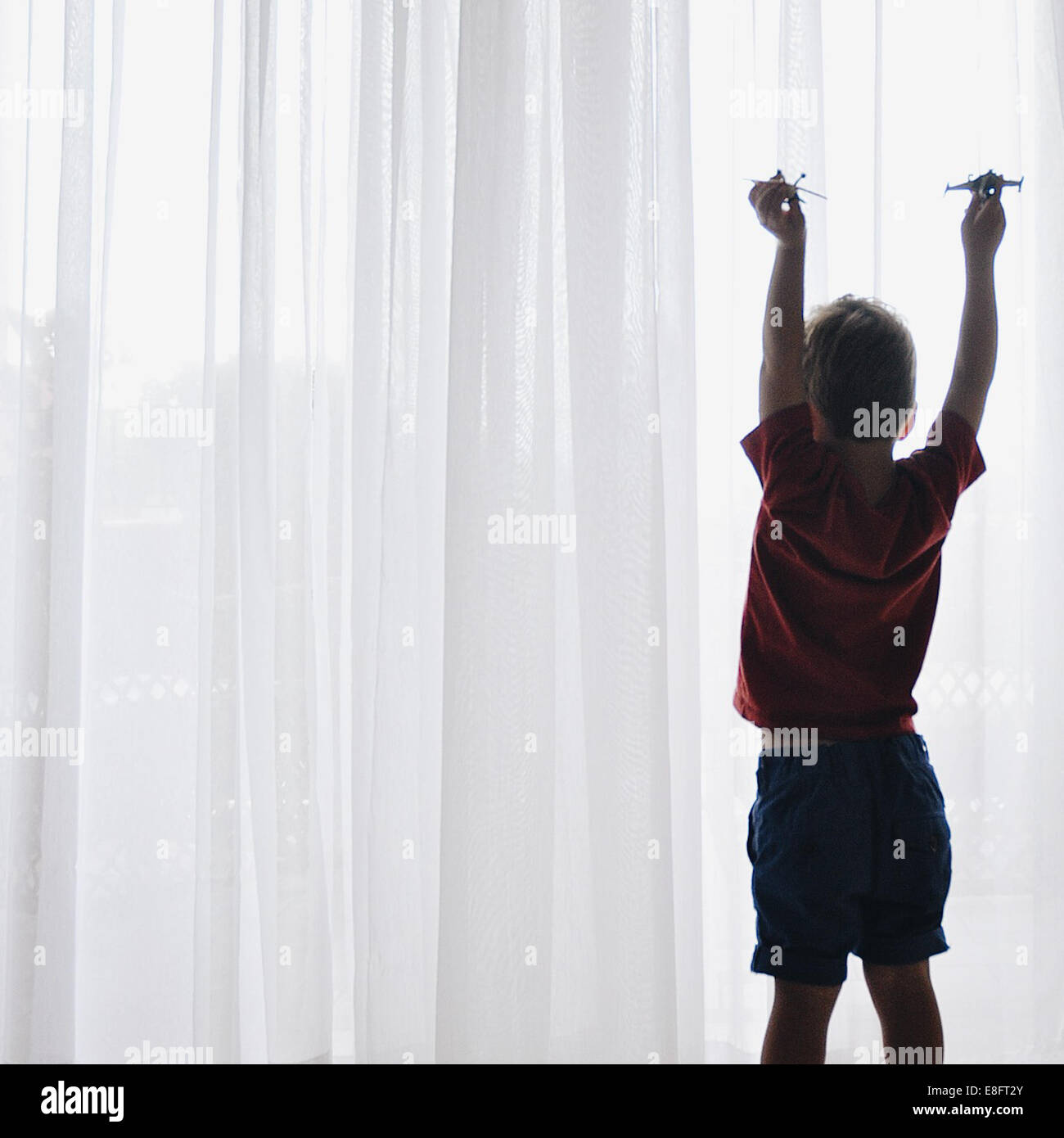 Boy standing by window playing with toy airplanes Stock Photo - Alamy