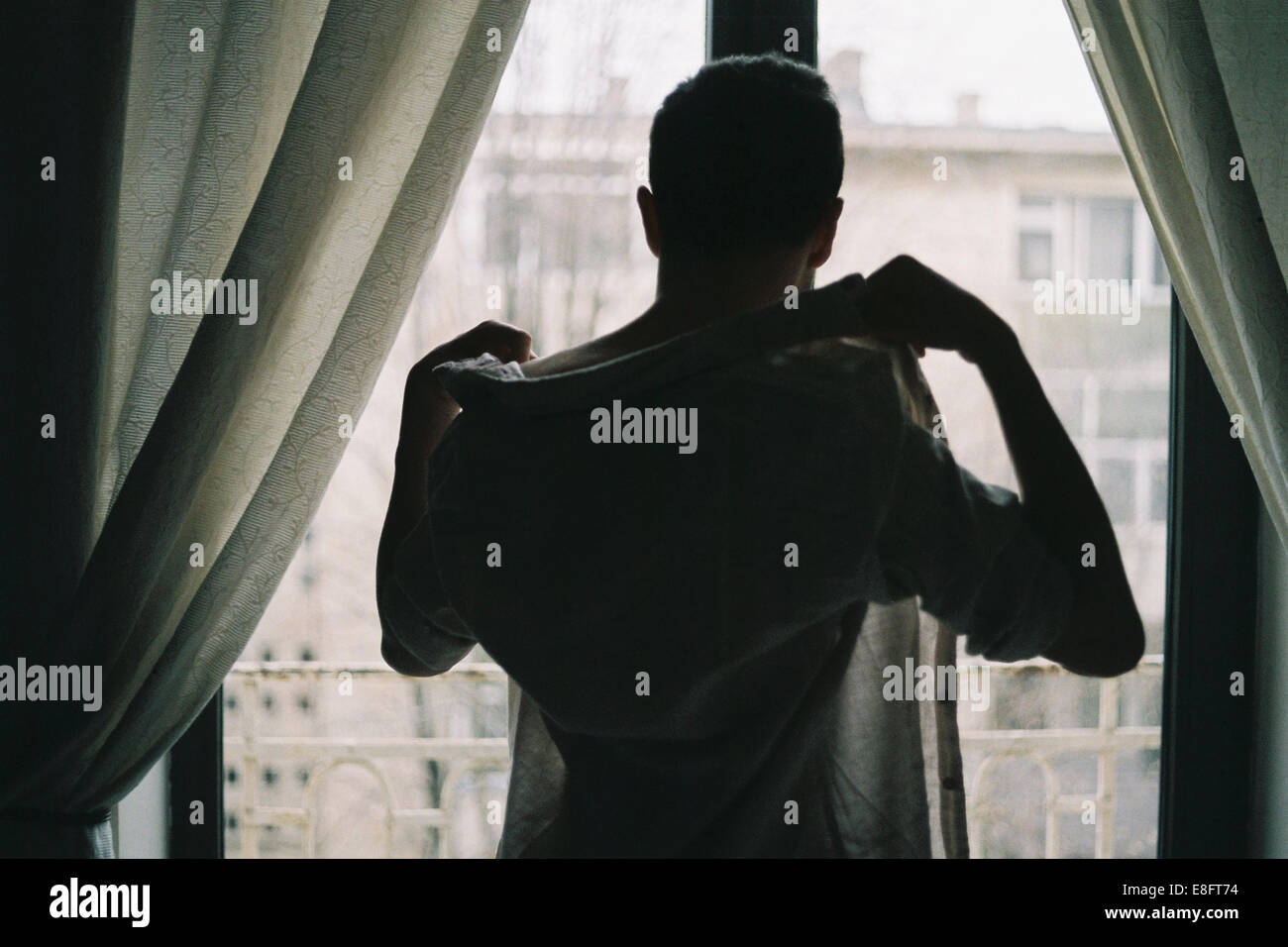 Man standing in front of a window getting dressed Stock Photo - Alamy