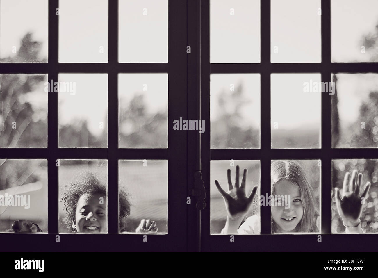 Two girls looking through a window Stock Photo - Alamy