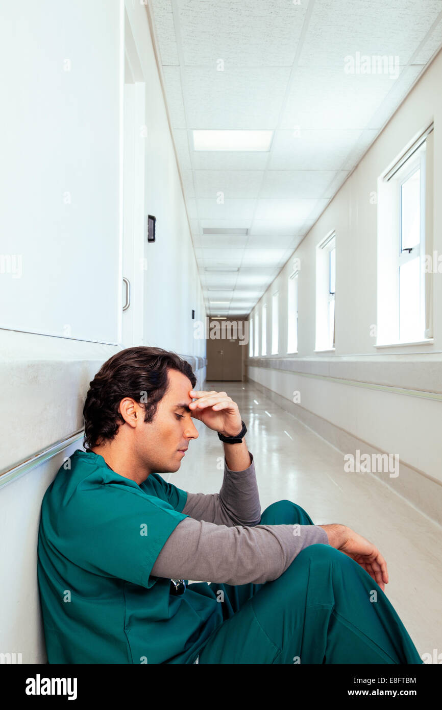 Tired male doctor sitting in hospital corridor with his hand on his ...