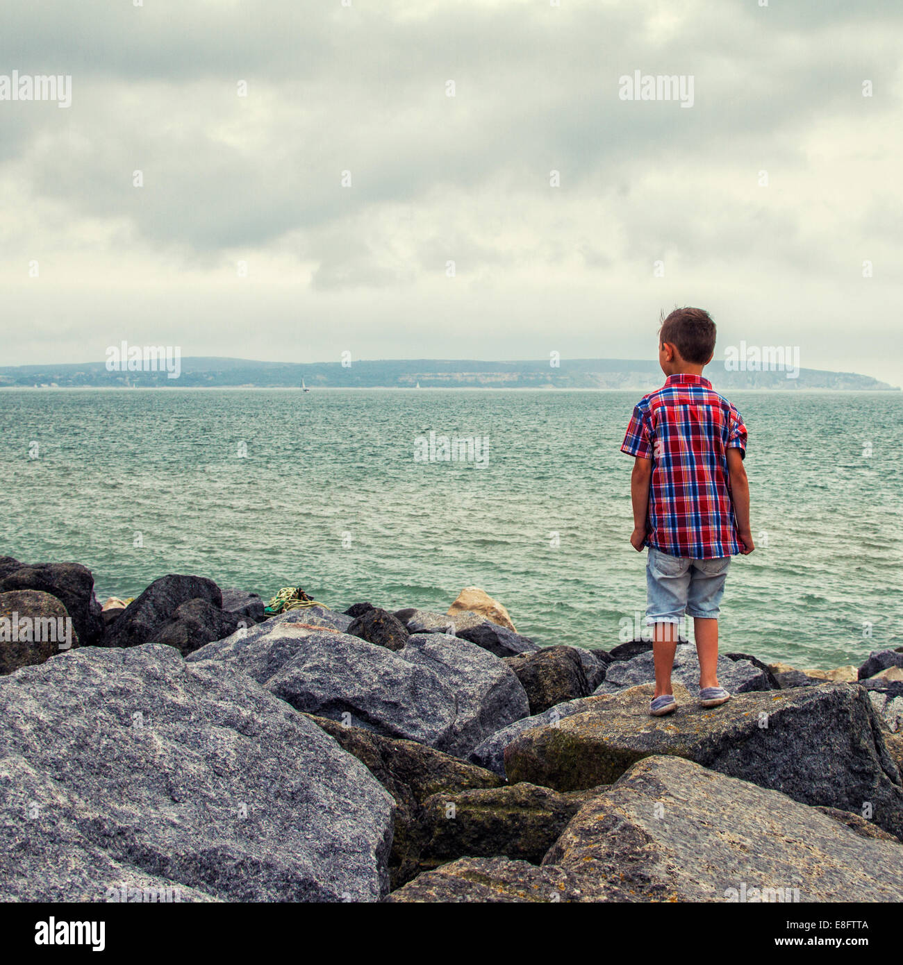 Boy standing on rocks looking at sea Stock Photo - Alamy
