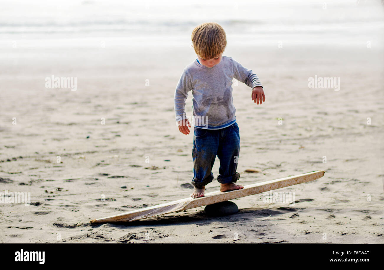 Boy standing on beach balancing on a wooden plank Stock Photo - Alamy