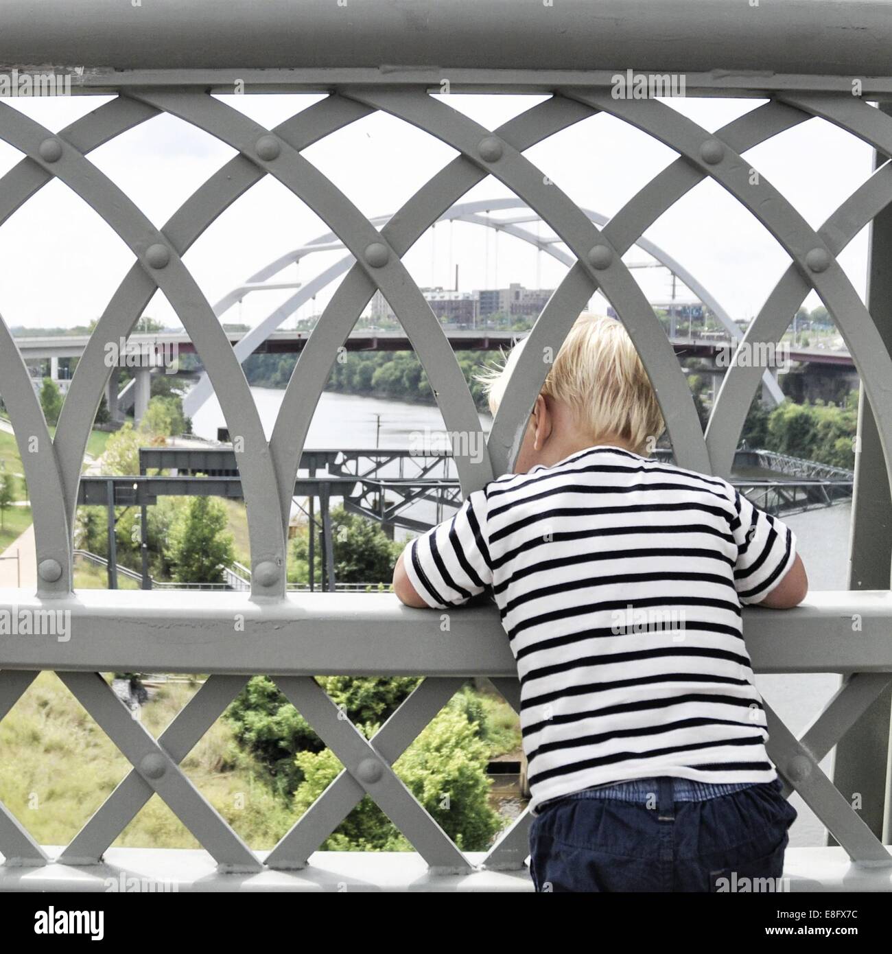 Boy standing on bridge looking through railings Stock Photo - Alamy