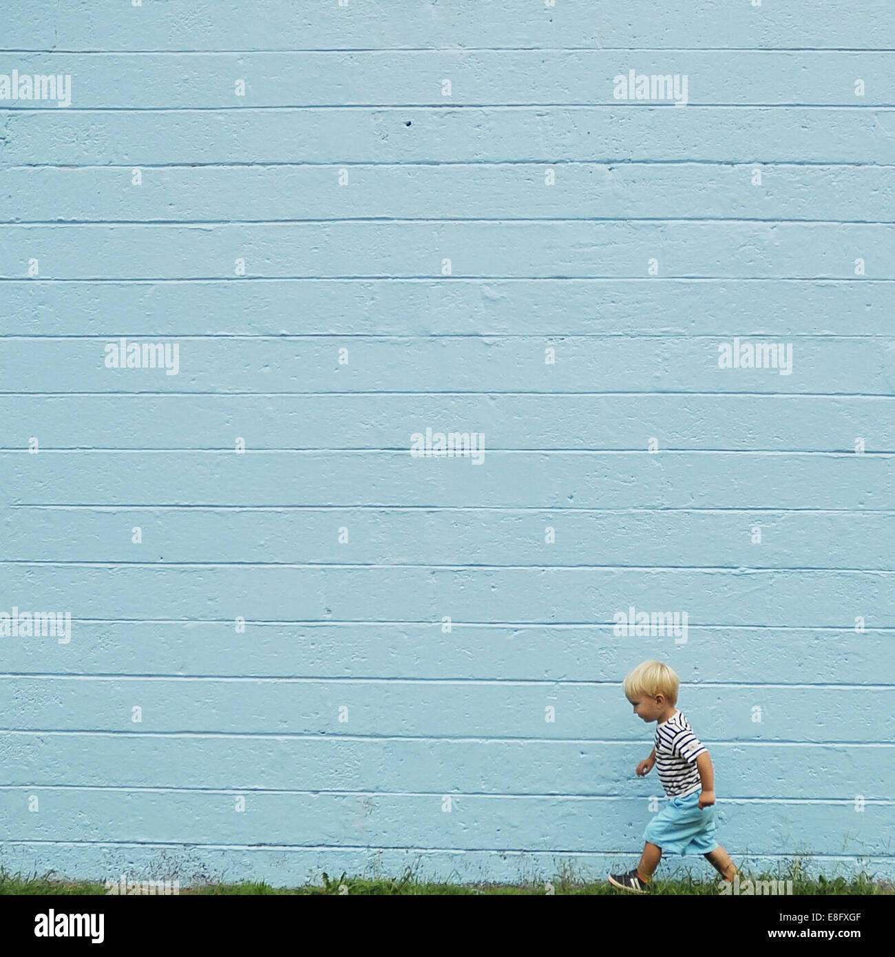 Boy walking past a blue wall Stock Photo - Alamy