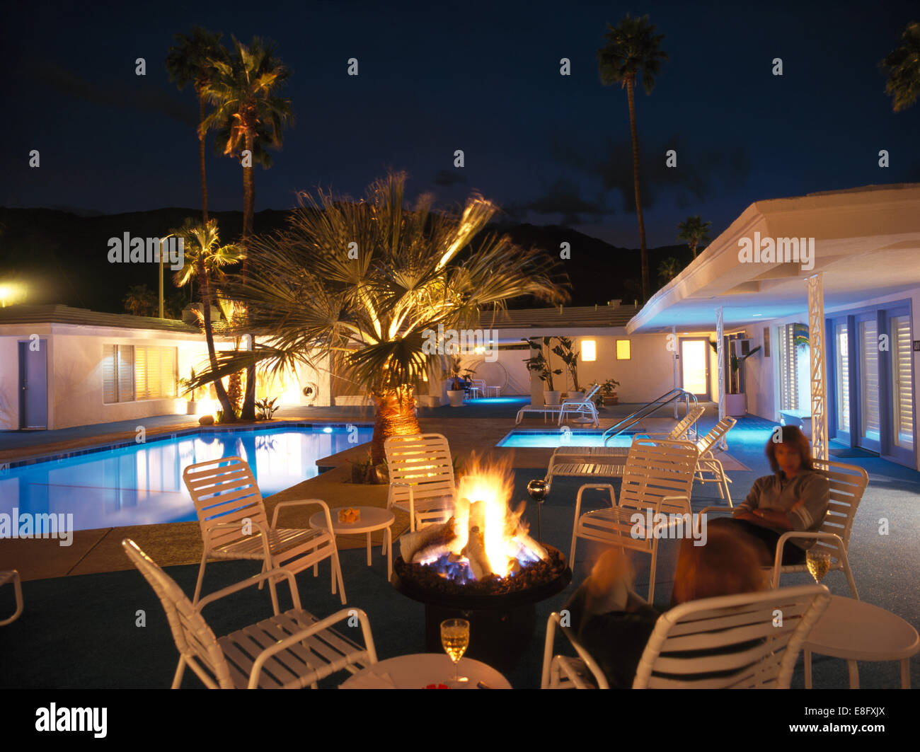 Two women sitting around fire pit on patio beside swimming pool of ...