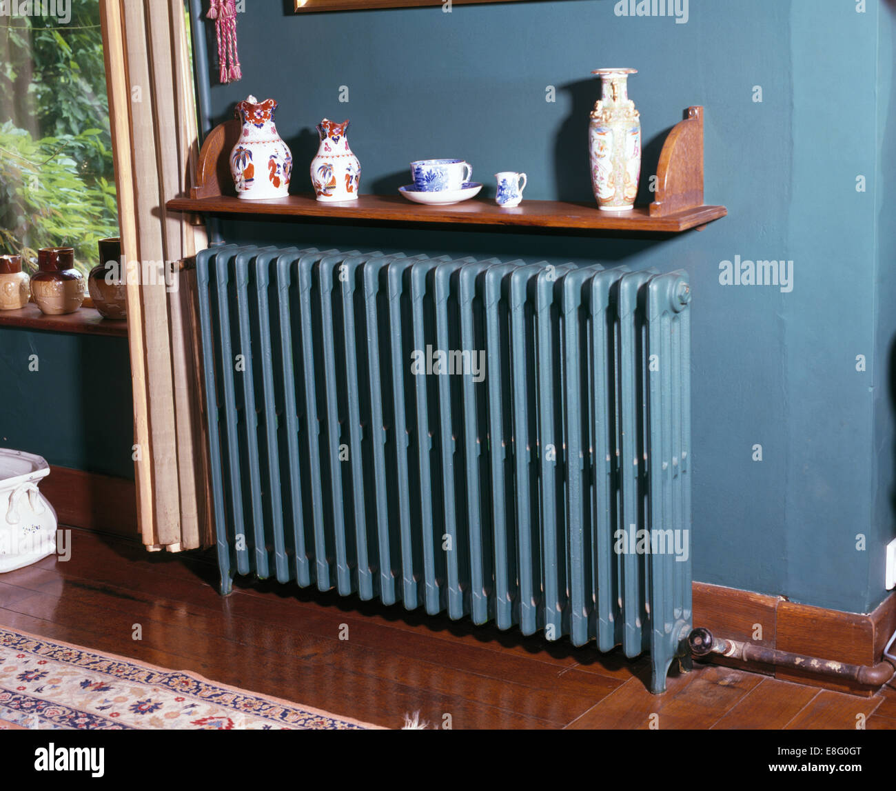 Close-up of turquoise painted radiator below wooden shelf with china ...