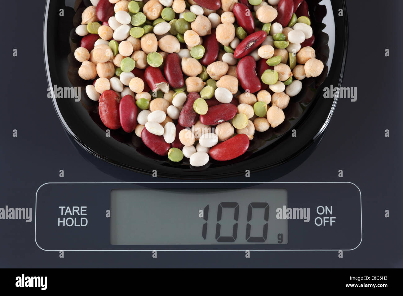 Mixed legume beans in a black plate on digital scale displaying 100 ...