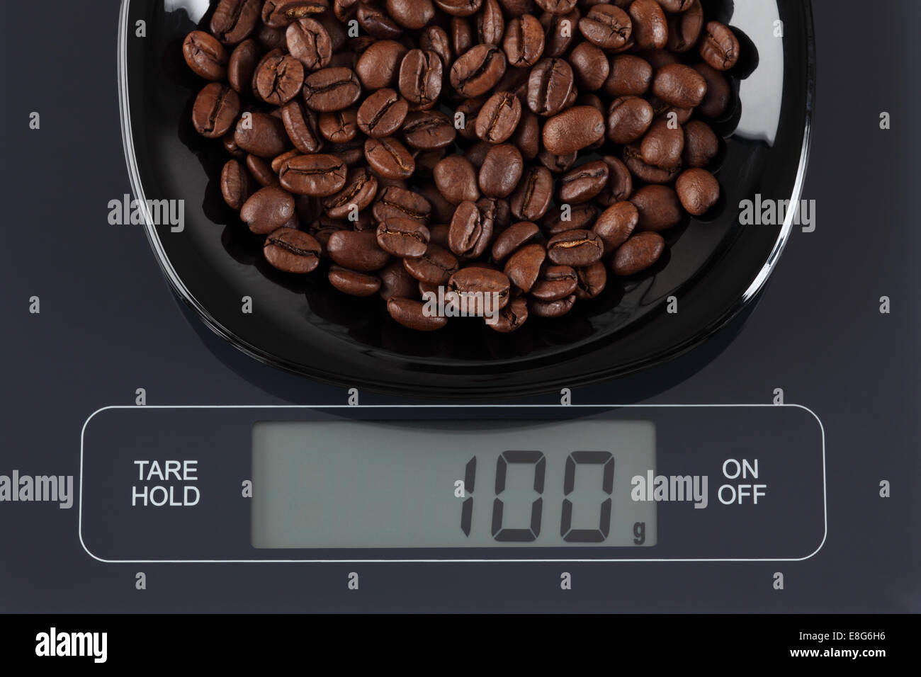Coffee beans in a black plate on digital scale displaying 100 gram ...