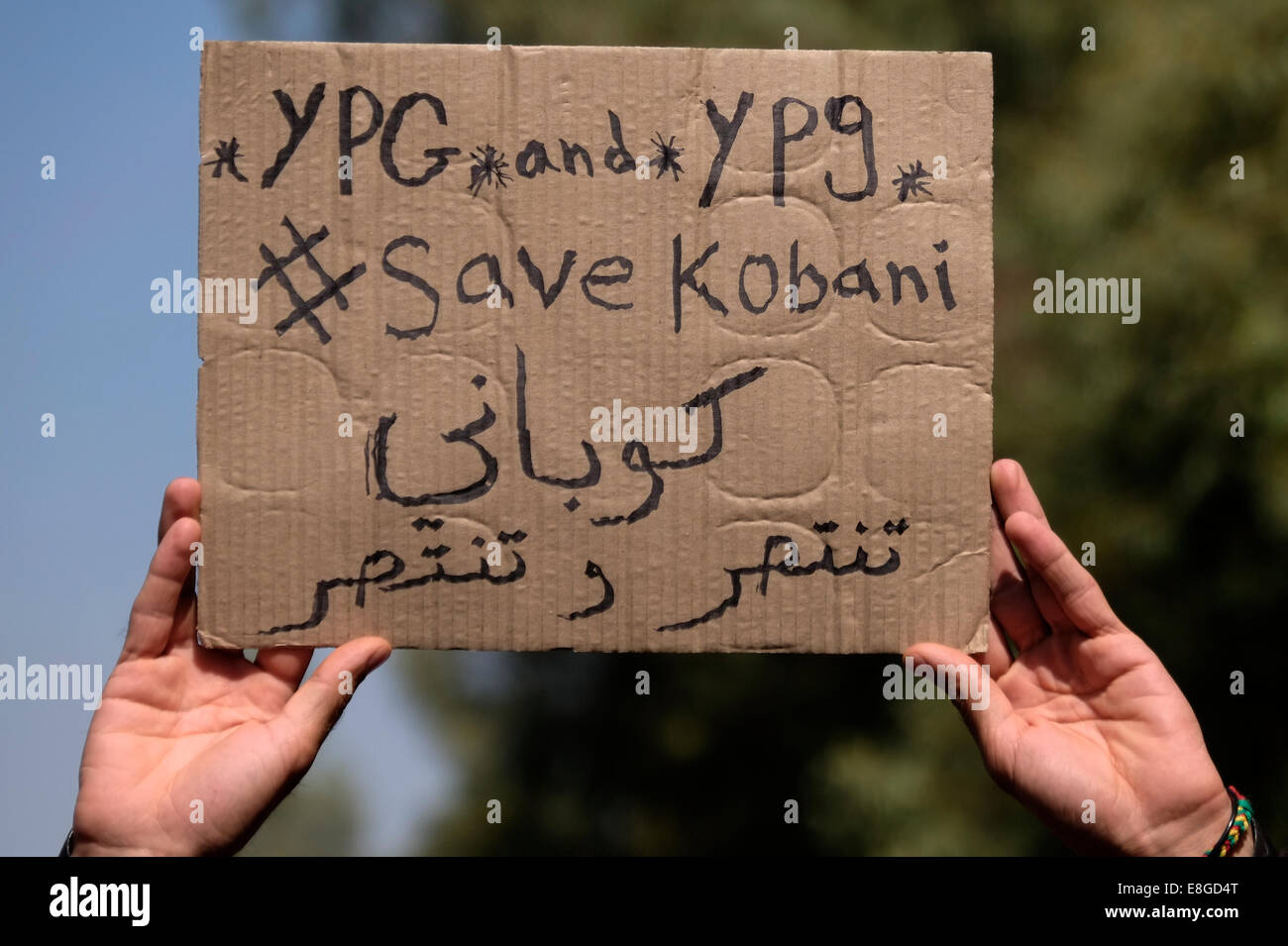 A Kurdish man holds a cardboard sign which reads "YPG save Kobani ...