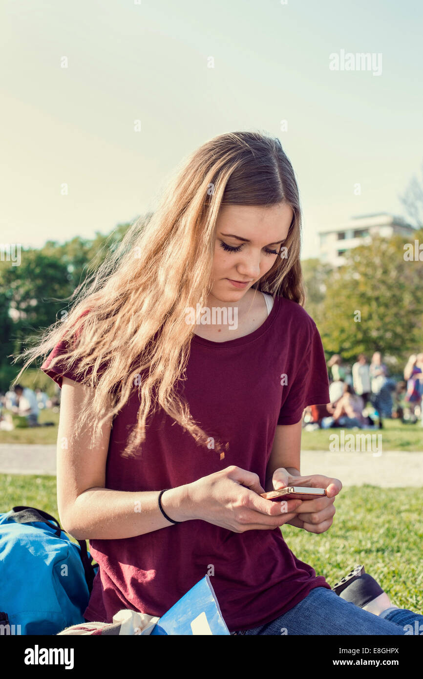 Female high school student text messaging on mobile phone at schoolyard ...