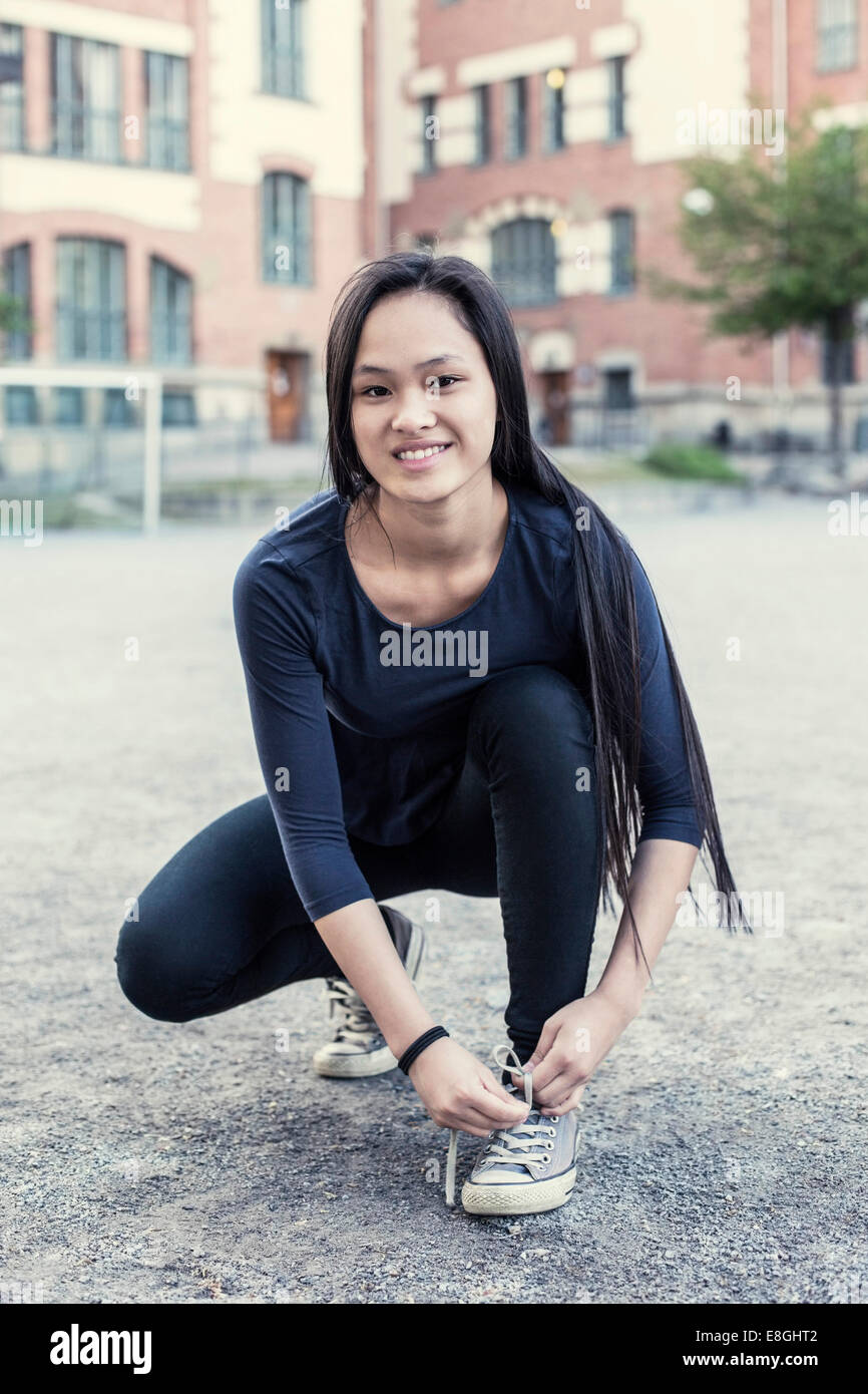 Full length portrait of female student tying shoelace on high school ...