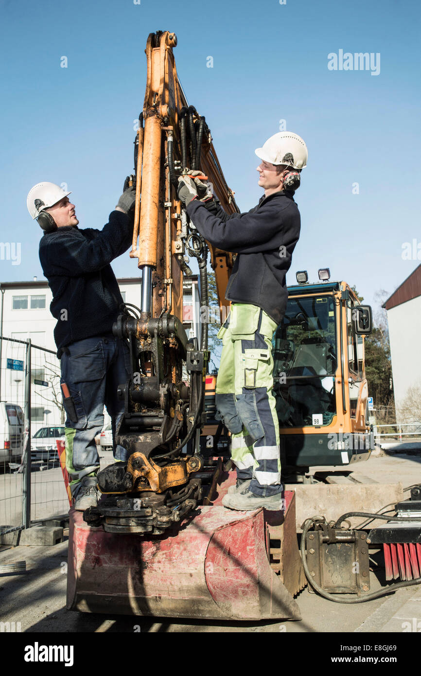 Side view of construction workers using excavator against blue sky ...