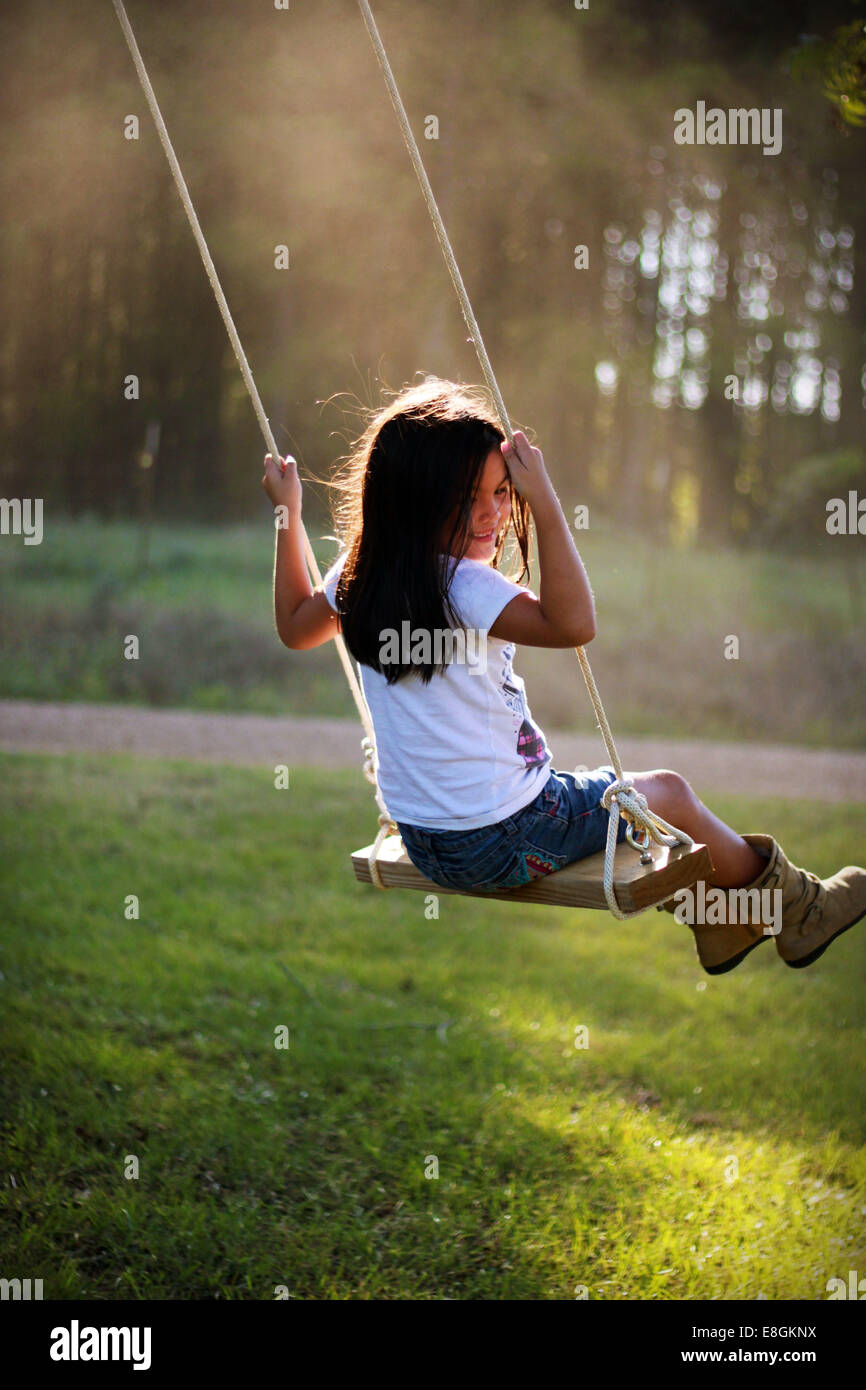 Smiling girl sitting on a rope swing in the garden, Mississippi, USA ...