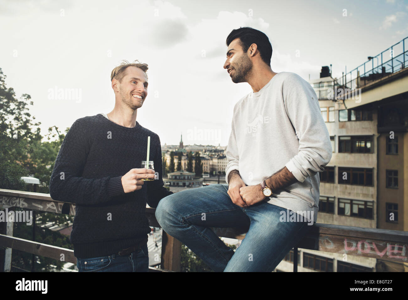 Happy male friends communicating on roof garden Stock Photo - Alamy