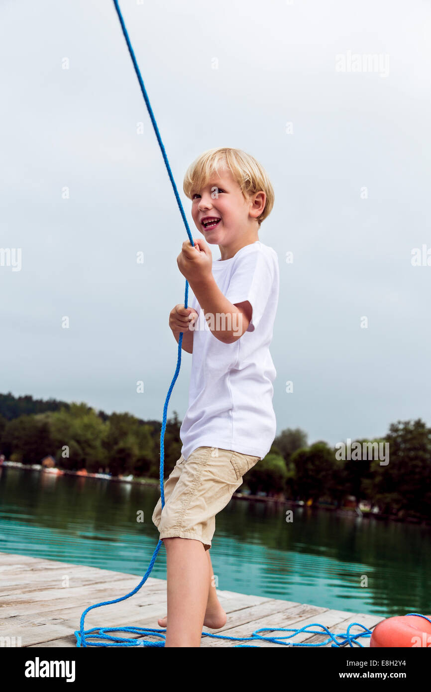 Portrait of smiling little boy standing on a jetty pulling a rope Stock ...