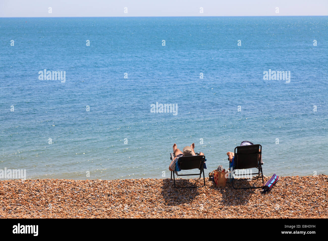 Two people in sun loungers on shingle beach by sea from behind Stock ...