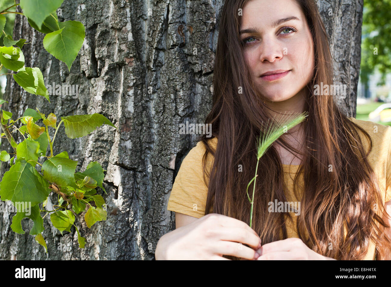 Portrait of young woman with spike in her hand sitting in front of tree ...