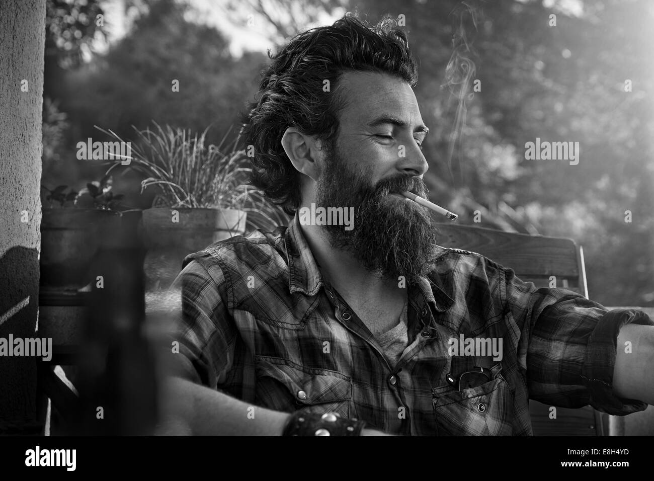 Man with full beard smoking cigarette on porch Stock Photo - Alamy