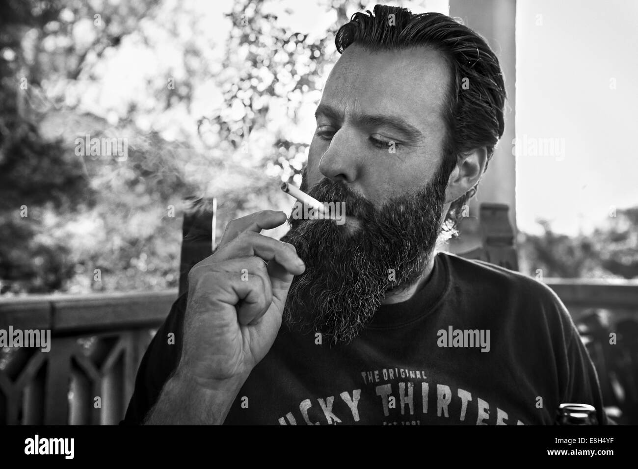 Man with full beard smoking cigarette on porch Stock Photo - Alamy