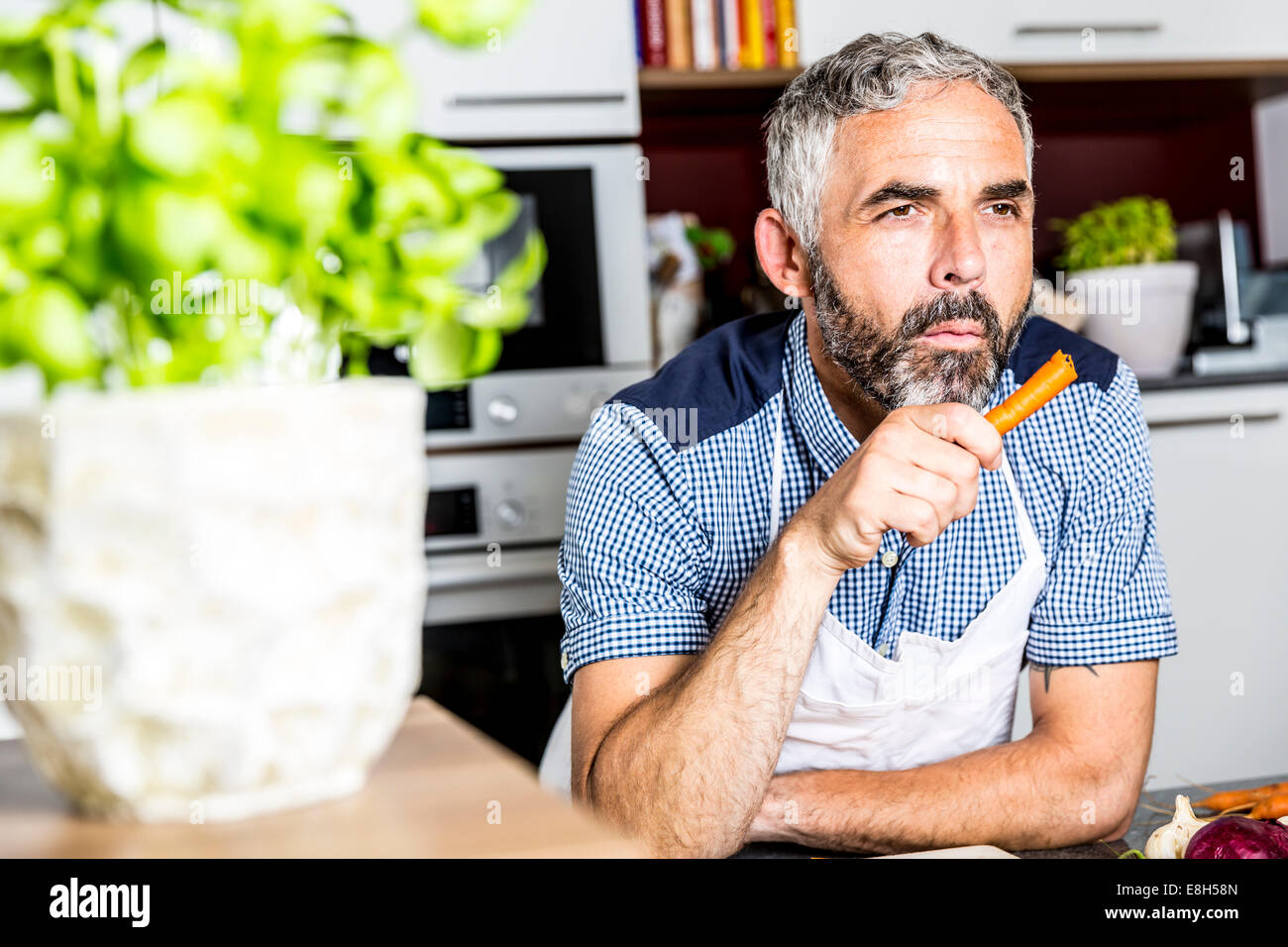 Austria, Man in kitchen eating carrot Stock Photo - Alamy