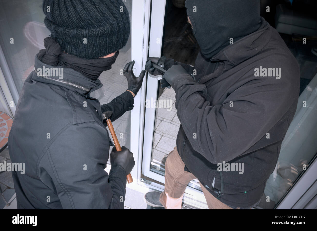 Two burglars opening terrace door of an one-family house with hammer ...
