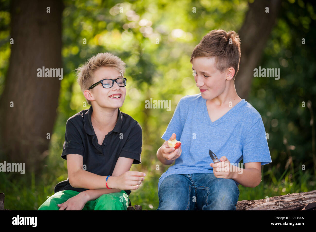 Two boys sitting on a tree trunk eating an apple Stock Photo - Alamy