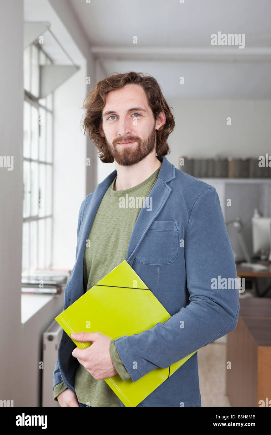 Portrait of smiling young man with file standing in an office Stock ...