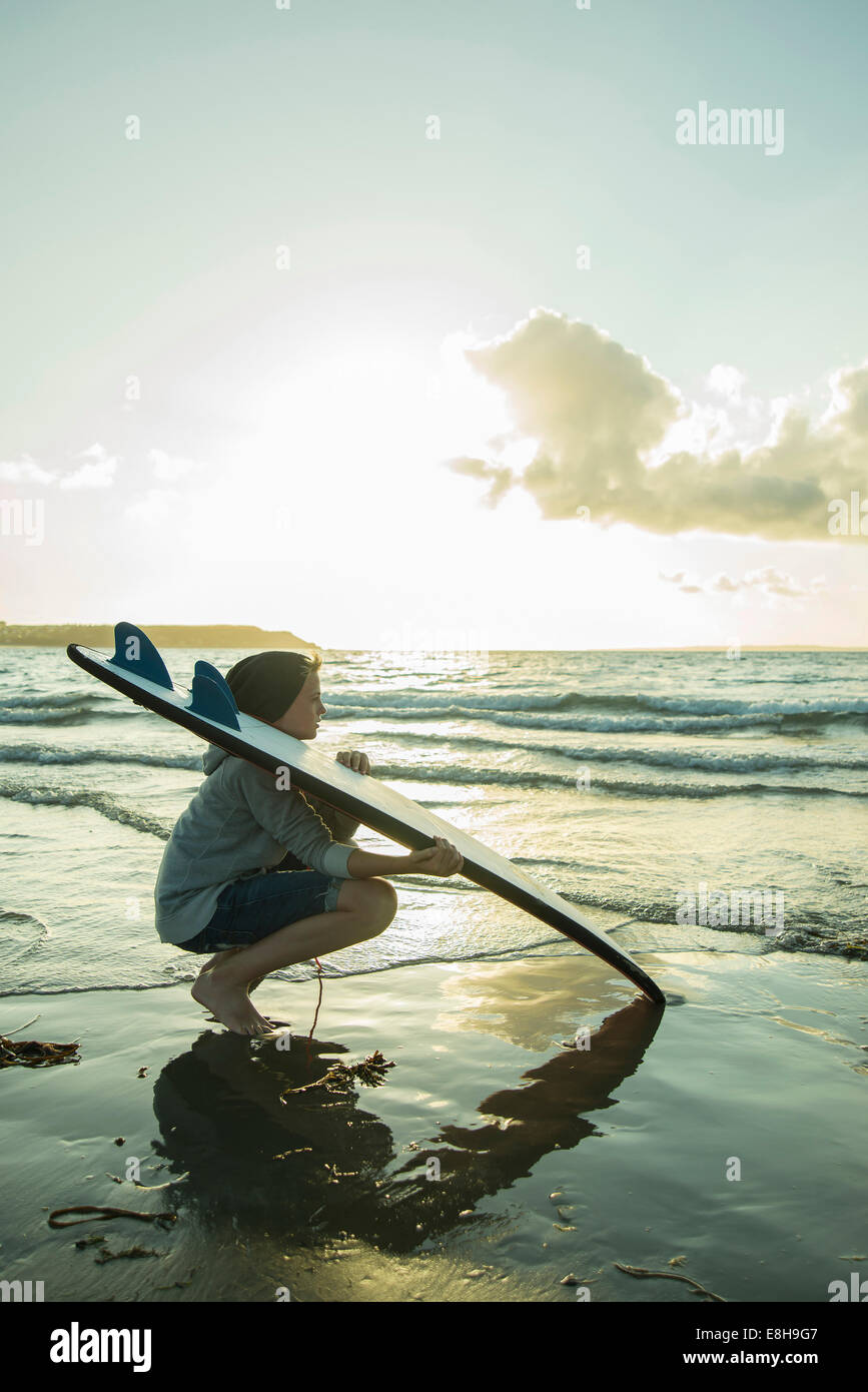 Teenage boy crouching at waterside of the sea with hir surfboard Stock ...