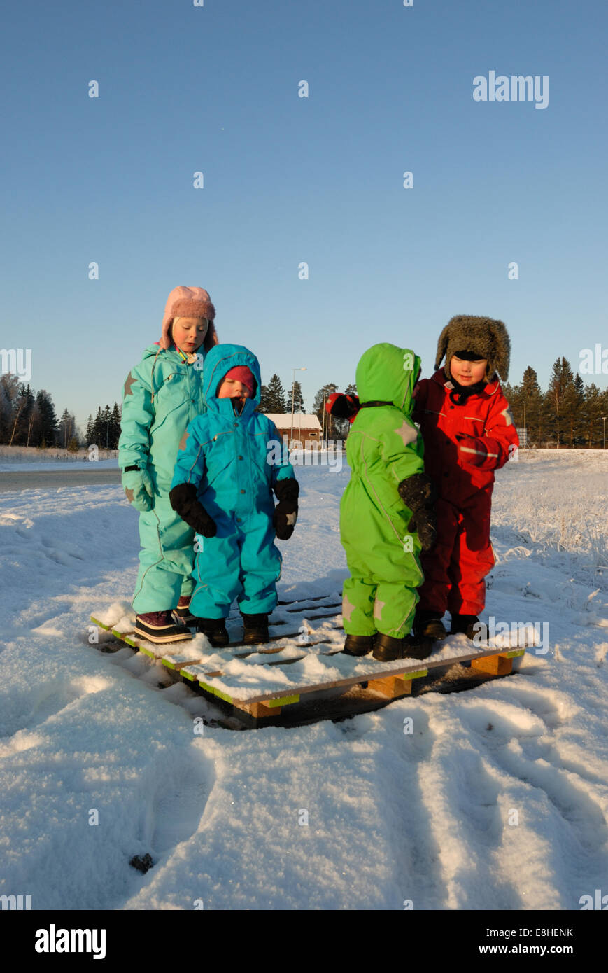 Children in colorful winter clothing standing on a discarded wooden ...