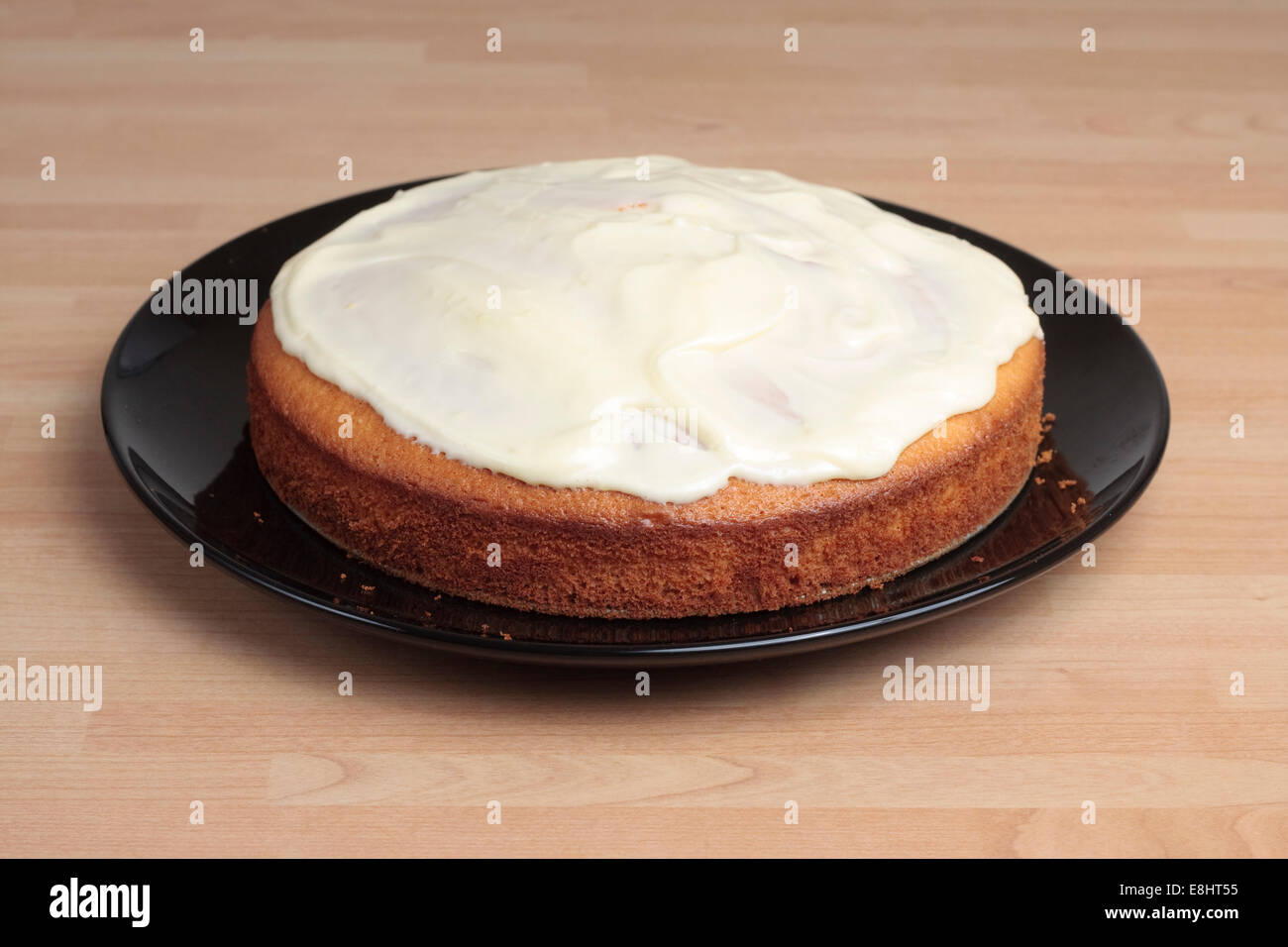 An iced lemon sponge cake on a black plate Stock Photo - Alamy