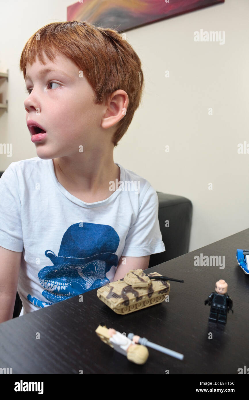 A five year old boy playing with small toys at the dinner table in a ...