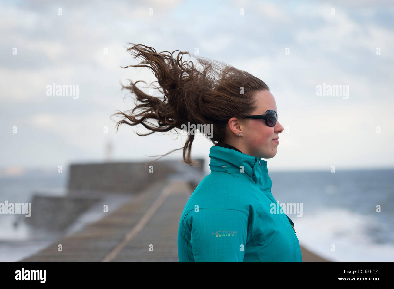 A young female girl stands facing into the wind with her hair blowing ...